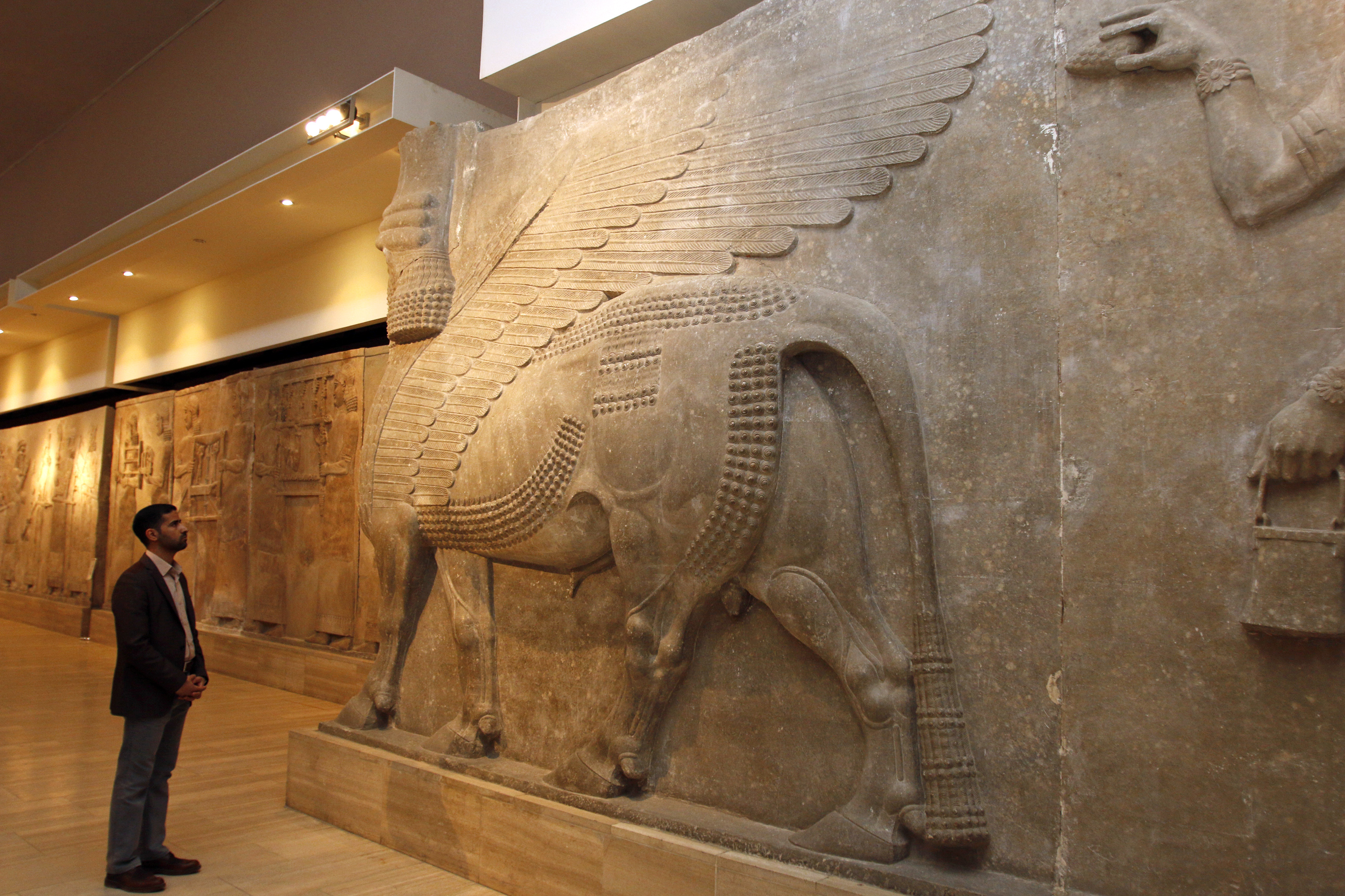 A man looks at an ancient Assyrian statue of a winged bull with a human ...